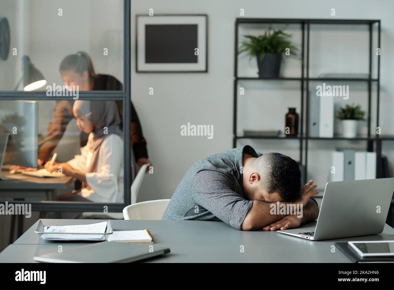 Young exhausted man keeping head on desk while sitting in front of ...