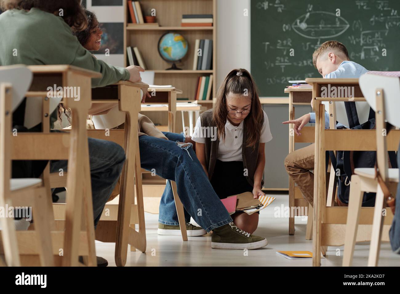 Cruel schoolkids laughing at their classmate standing on knees in aisle ...