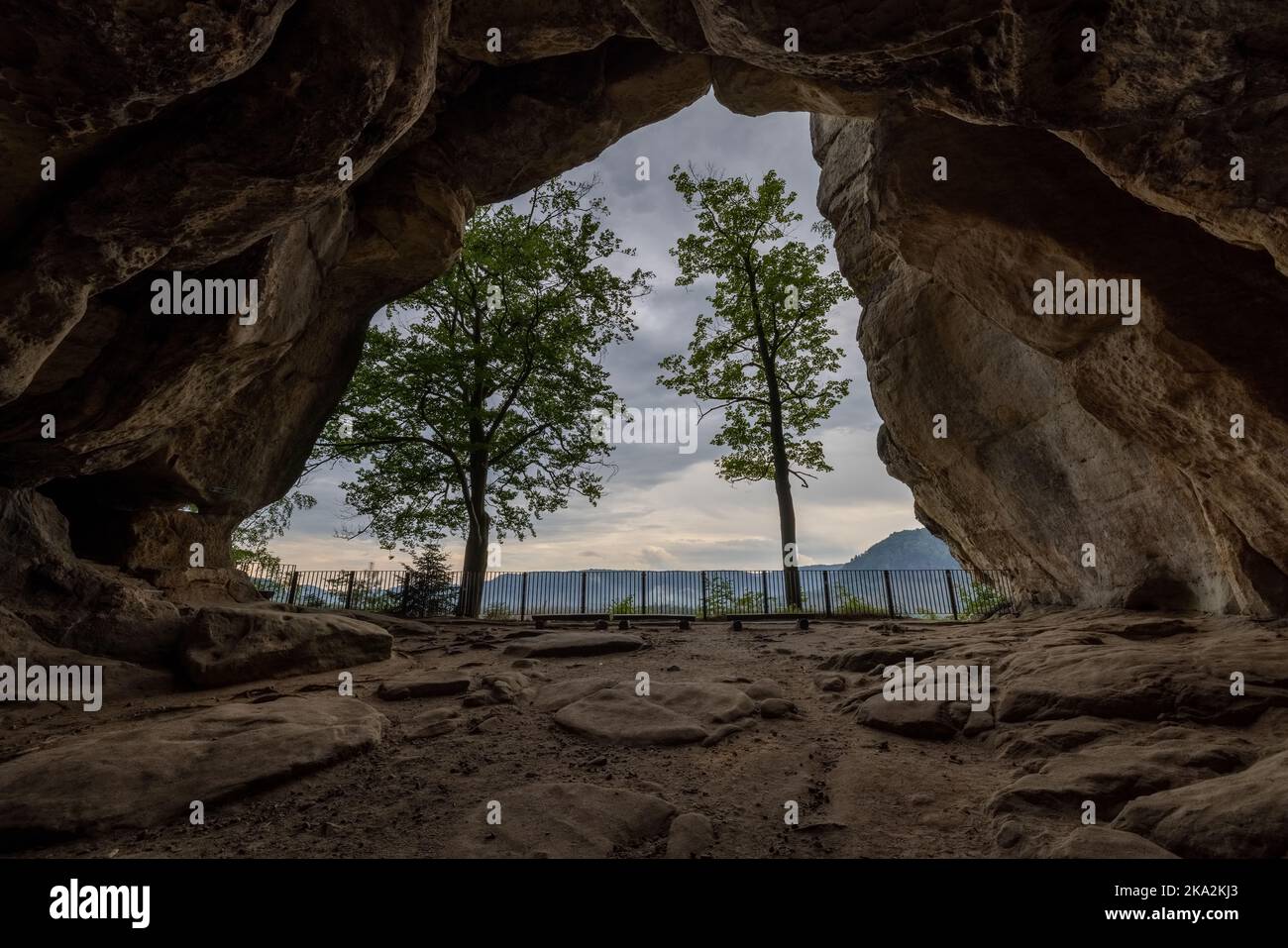 Two green trees visible through the arch of a cave Stock Photo - Alamy