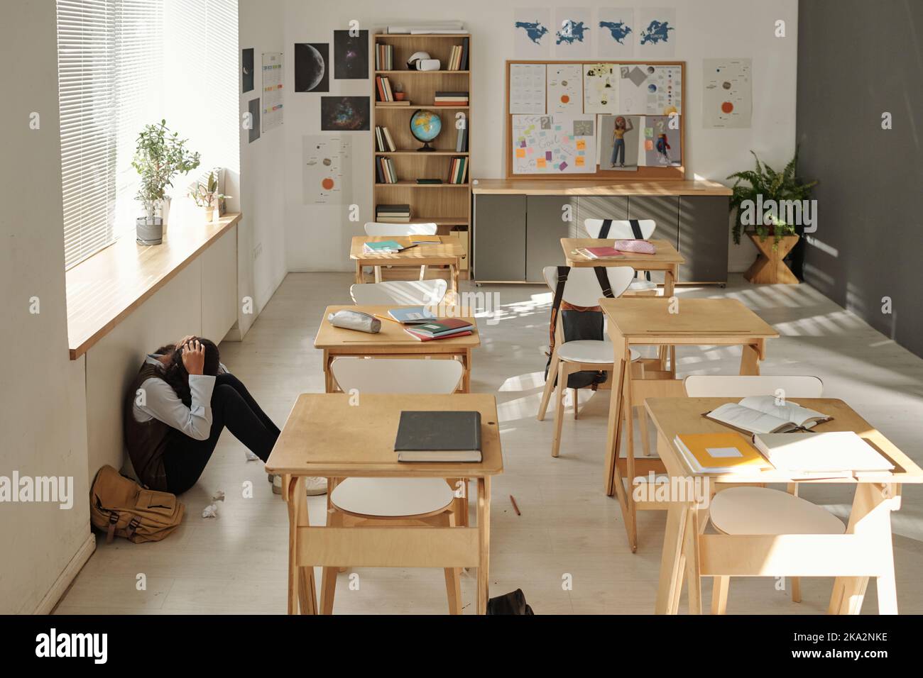 Interior of classroom and upset schoolgirl sitting on the floor between ...