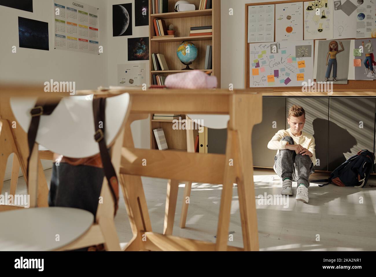 Lonely and unhappy schoolboy sitting on the floor of empty classroom ...