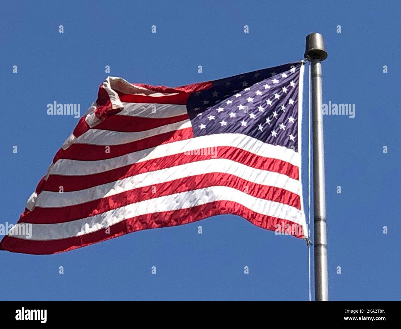 The American flag on a metal flag pole waving high on the air in blue ...