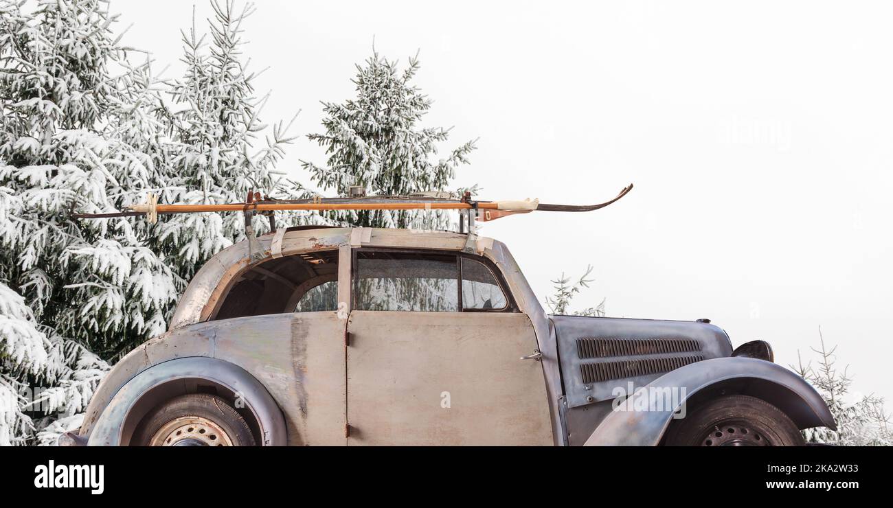 Vintage weathered car with skis attached to a roof rack in front of ...