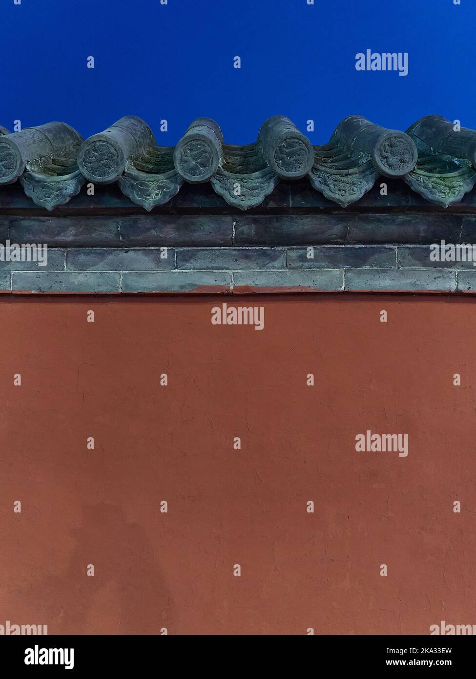 A vertical shot of a red Chinese temple wall with old roof tiles ...