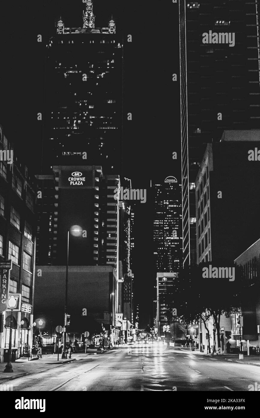 A vertical grayscale shot of skyscrapers illuminated by lights in the ...