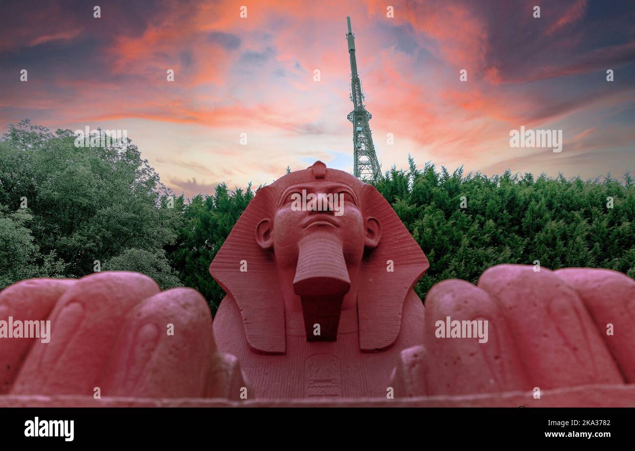 A closeup of a sphinx sculpture in a park with a transmission tower in ...