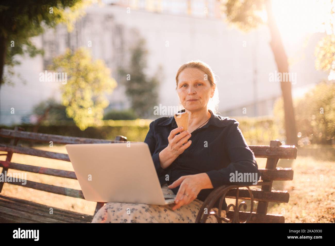 Mature business woman eating ice cream using laptop computer in park ...