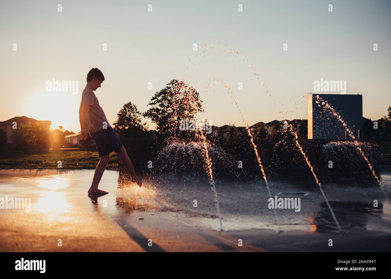 Boy playing in water fountains at a splash pad on summer evening Stock ...