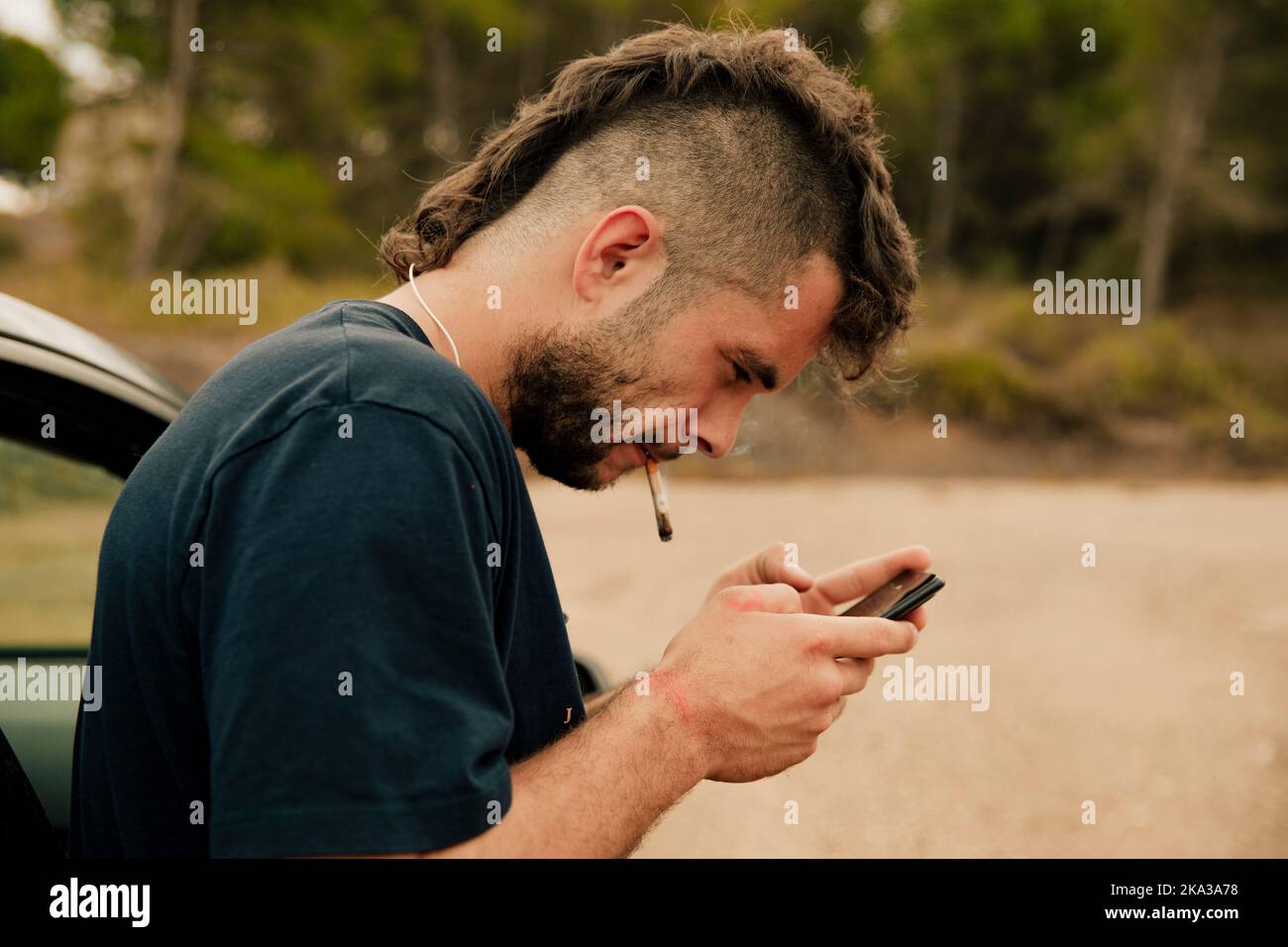 Young guy smoking a marijuana joint while looking at his smartphone ...