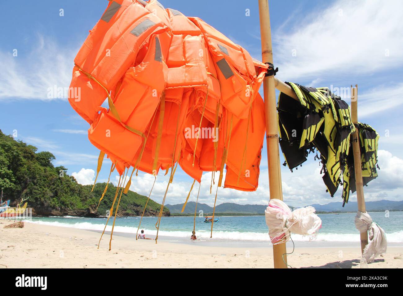 A bunch of orange and yellow life jackets on hanging on a bamboo pole ...