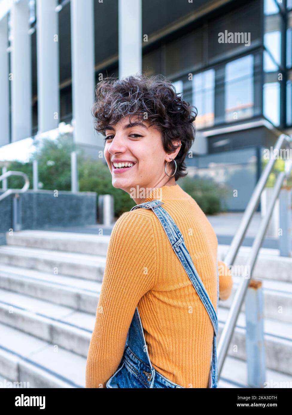 Side view ethnic female in denim overall looking over shoulder with ...
