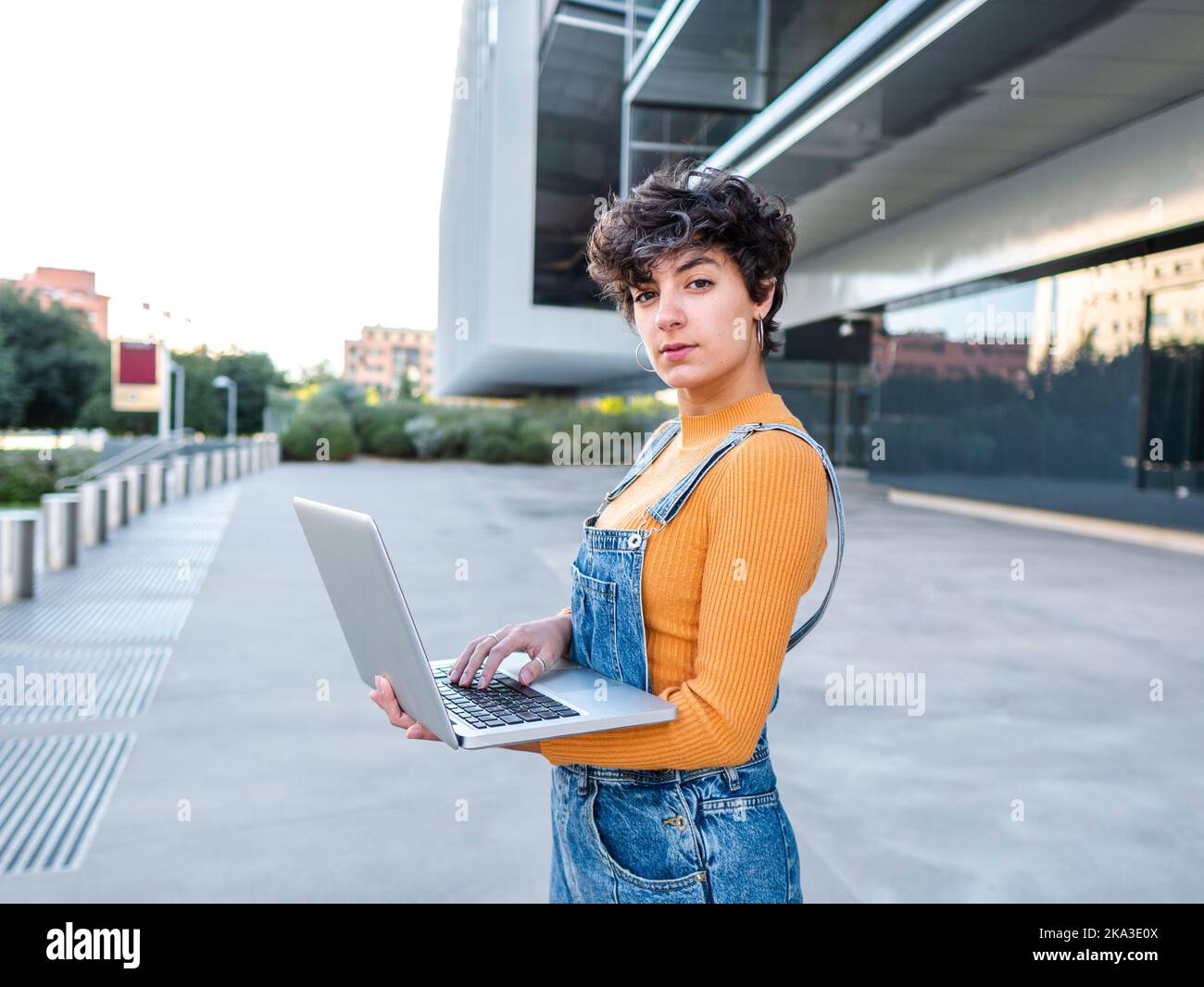 Side view of young female freelancer with short curly hair in denim ...