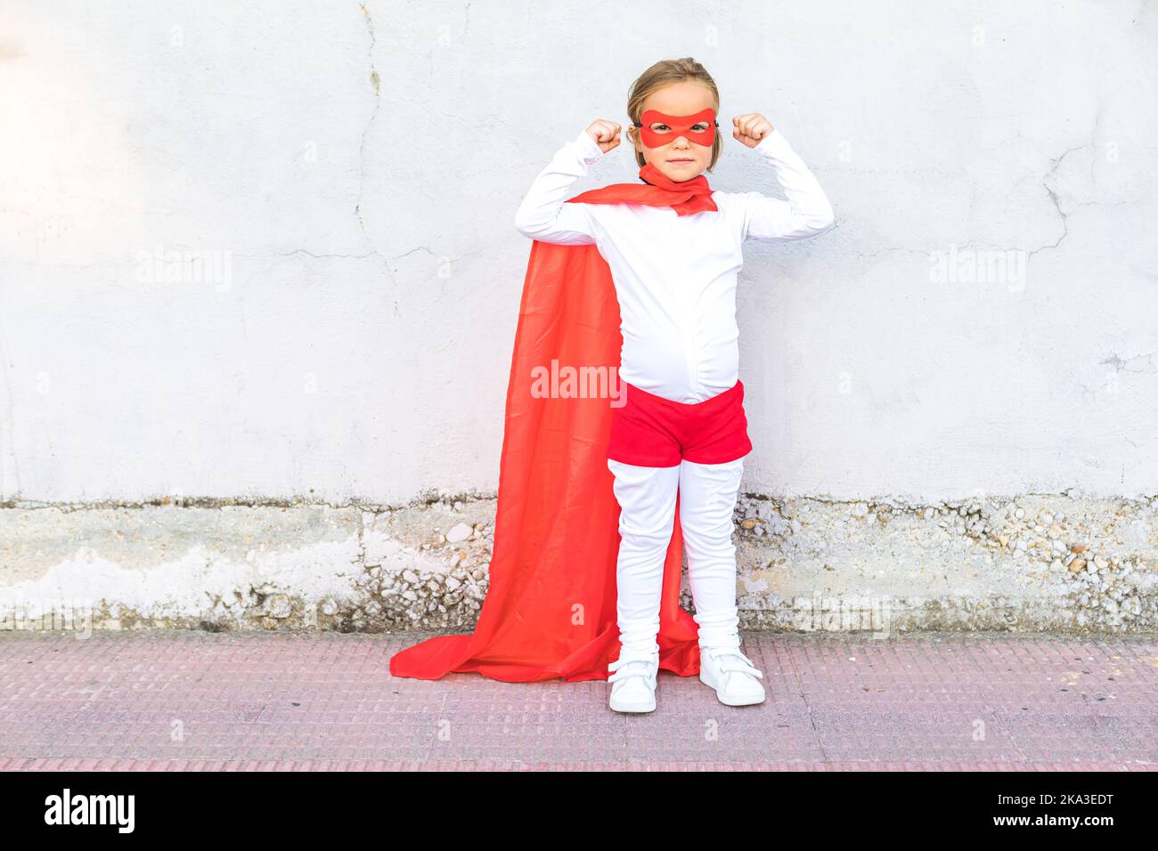 Full body of adorable little girl in superhero costume and mask flexing ...