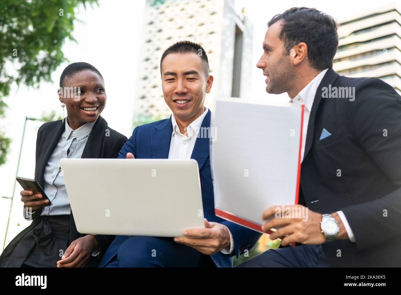 Group of smiling multiracial coworkers in formal suits sitting on bench ...