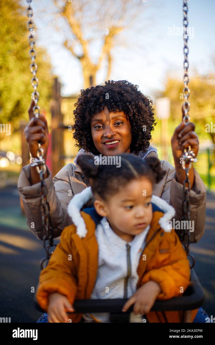 Glad African American mother with curly hair grasping chains of swing ...