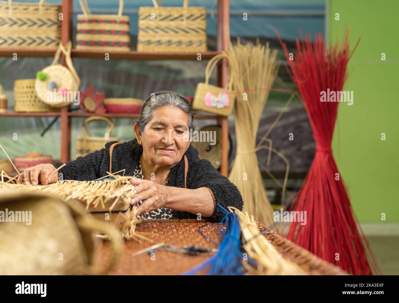 Focused elderly Hispanic female weaving basket from grass while sitting ...