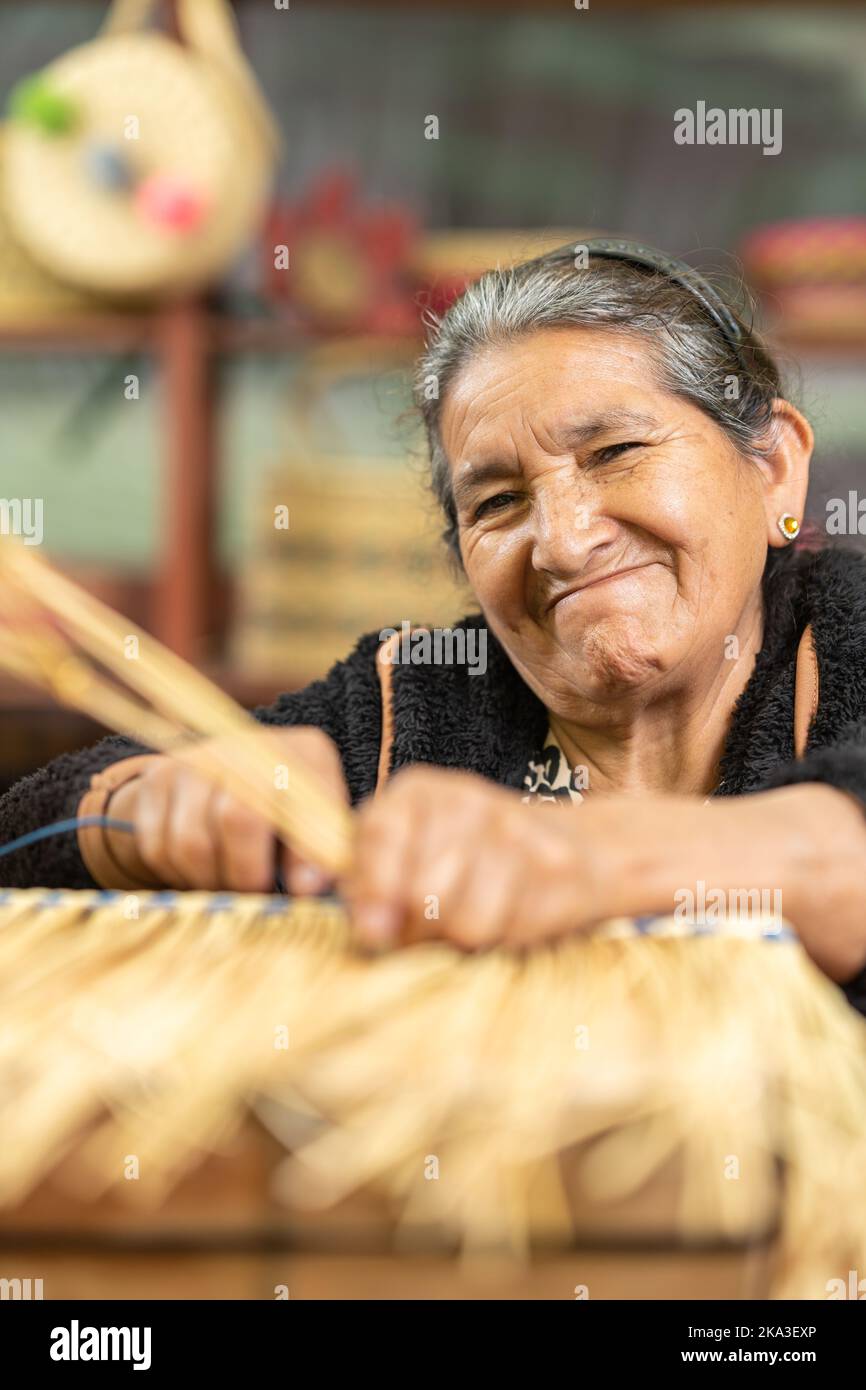 Focused elderly Hispanic female weaving basket from grass while sitting ...