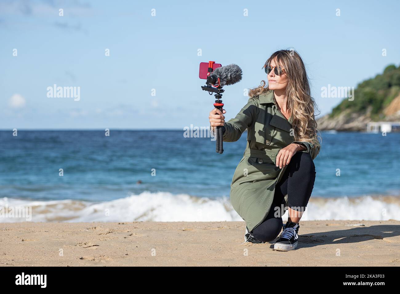 Young woman with long hair in casual trench coat sitting on haunches on ...