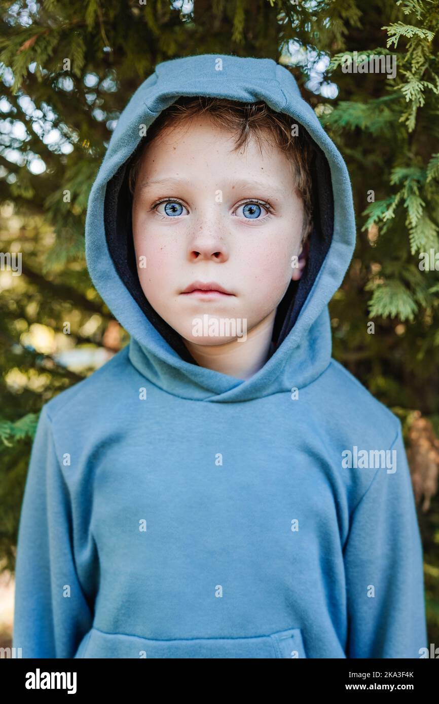 Blue eyed preteen kid with hood on head looking at camera against ...