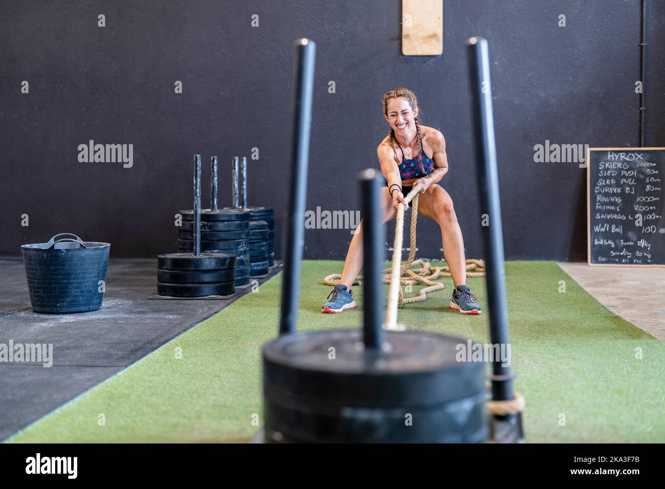 Full body cheerful female athlete smiling and pulling rope tied to ...
