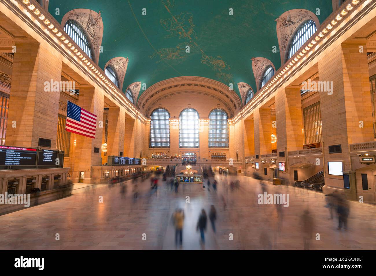 People walking in hall of Grand Central Terminal with USA flag hanging ...
