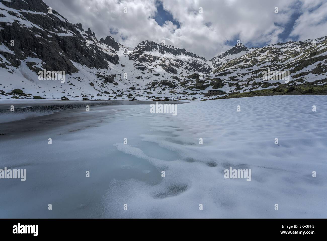 Frozen lake water with snow covered shoreline and dark rocky mountains ...