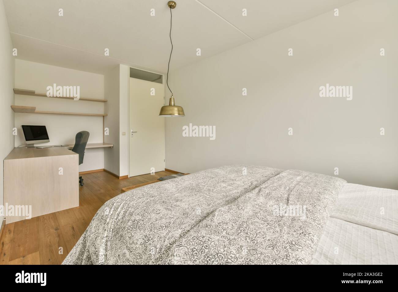 Comfortable bed with white walls next to a desk with computer Stock ...