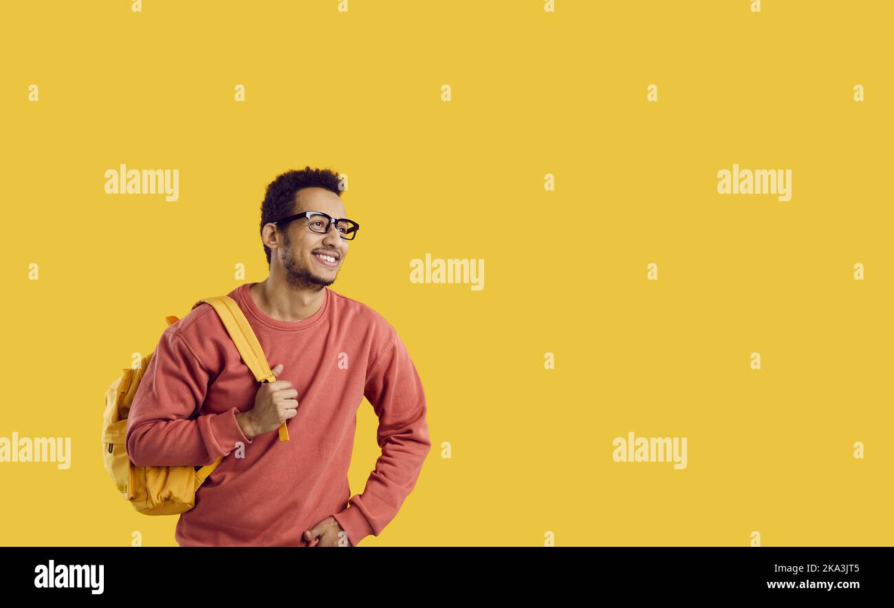 Happy black college or university student with backpack on yellow copy ...