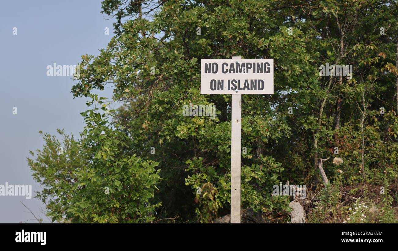 A no camping sign on the shore of island with green trees on the ...