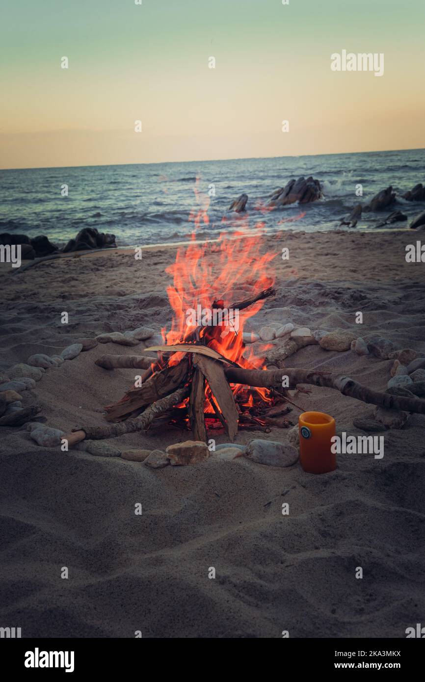 A vertical shot of a small camp fire on the beach by the water and a ...