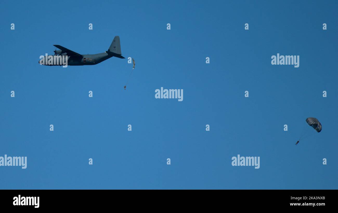 A military personnel parachuting from an RAAF aircraft in blue sky ...