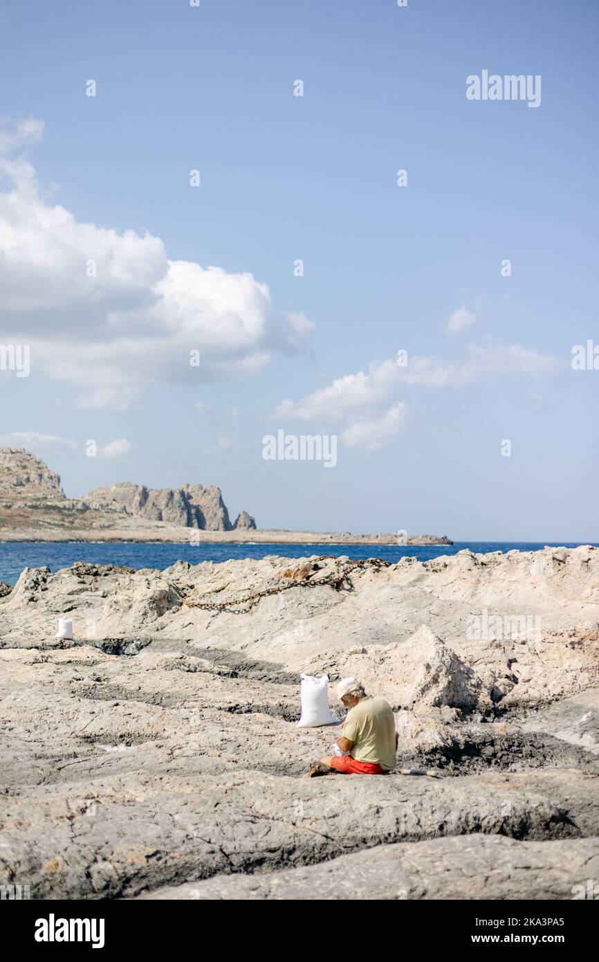A vertical shot of a male collecting sea salt at Elafonis beach in ...