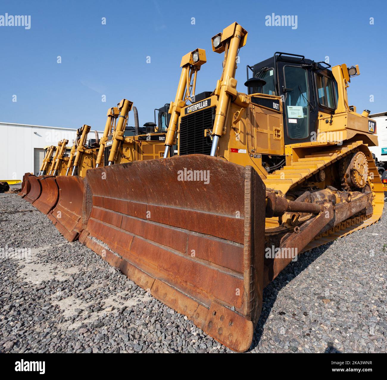 A row of bulldozers with blades and lift cylinders in a clear blue sky ...