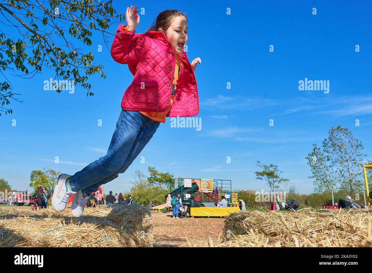 Pretty girl jumping over the hay stacks at a farm fair on Halloween ...