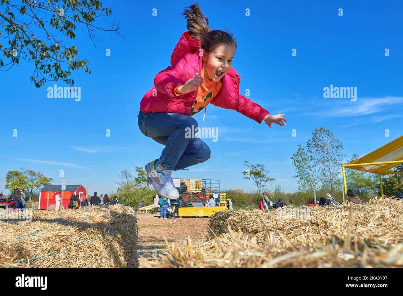 Pretty girl jumping over the hay stacks at a farm fair on Halloween ...