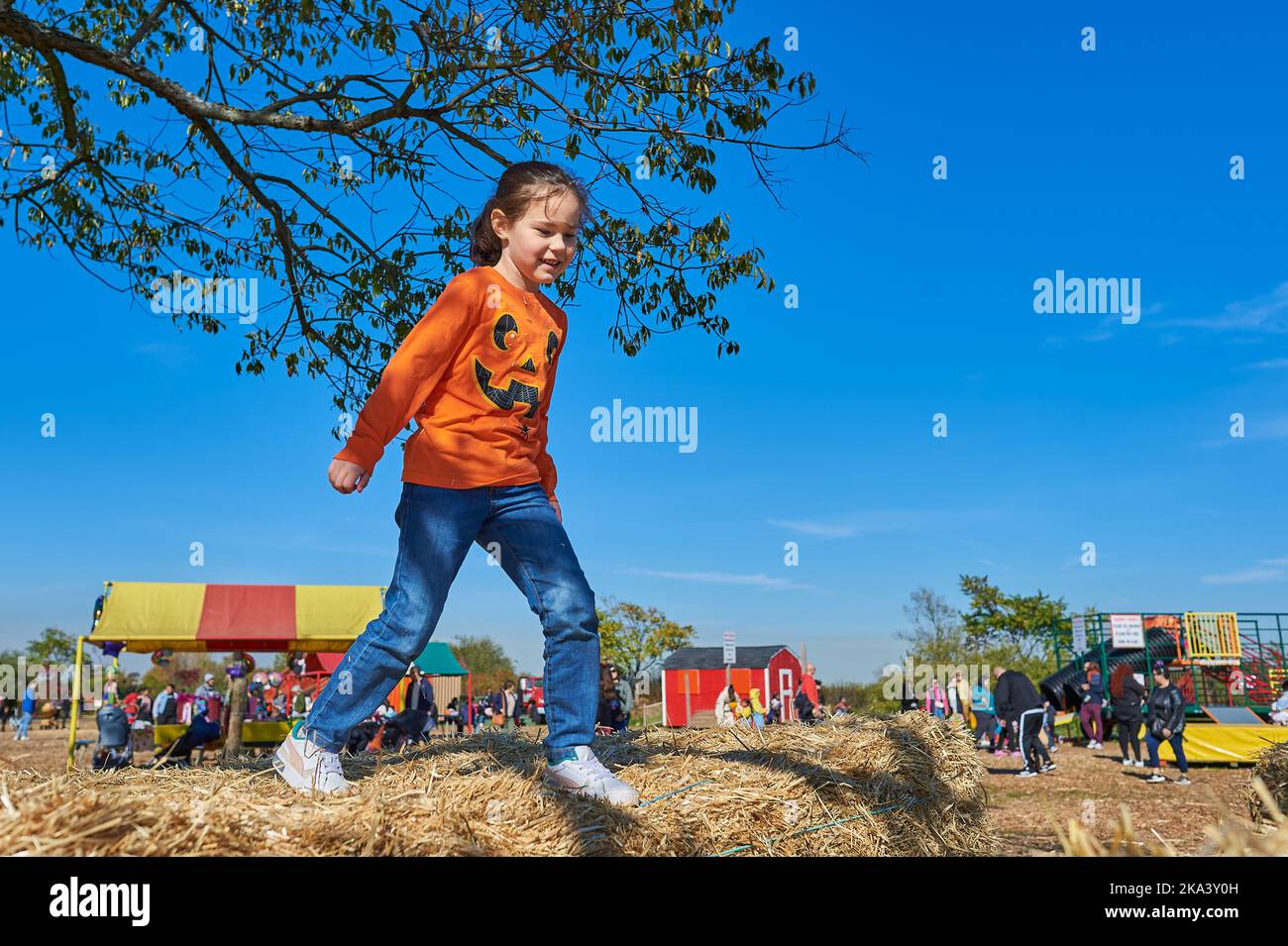 Pretty girl jumping over the hay stacks at a farm fair on Halloween ...