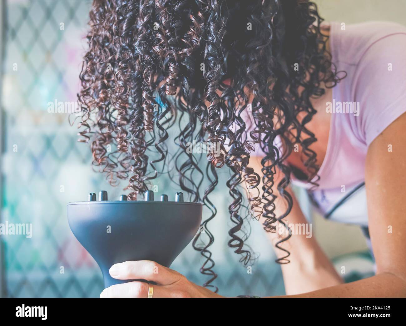 Close-Up of a woman bending over and drying her curly hair with a hair ...