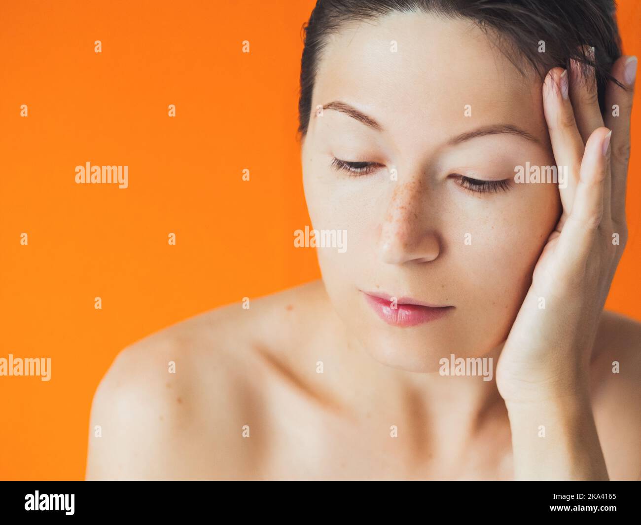 Portrait of woman with freckles on orange monochrome background. No ...