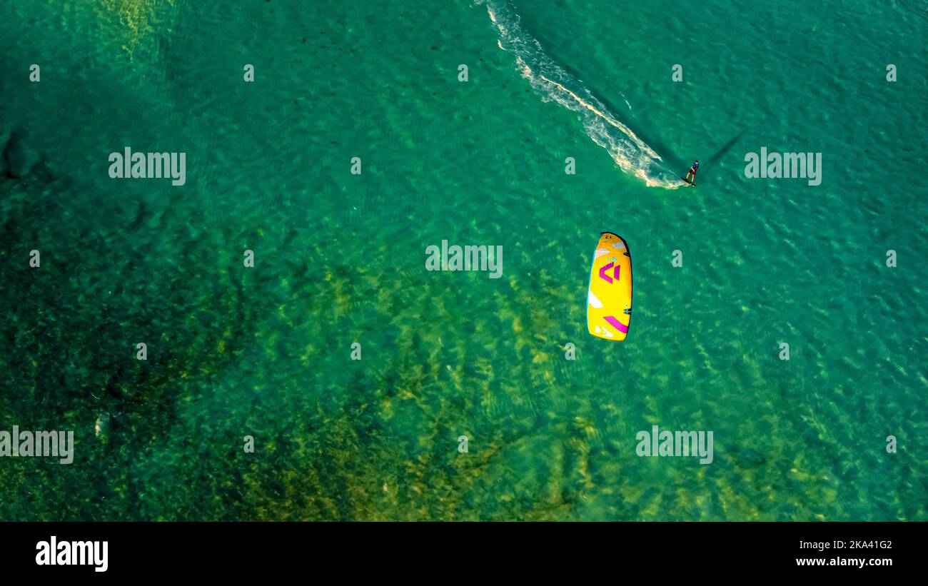 An aerial drone shot of the calm waters of the ocean and a kite surfer ...