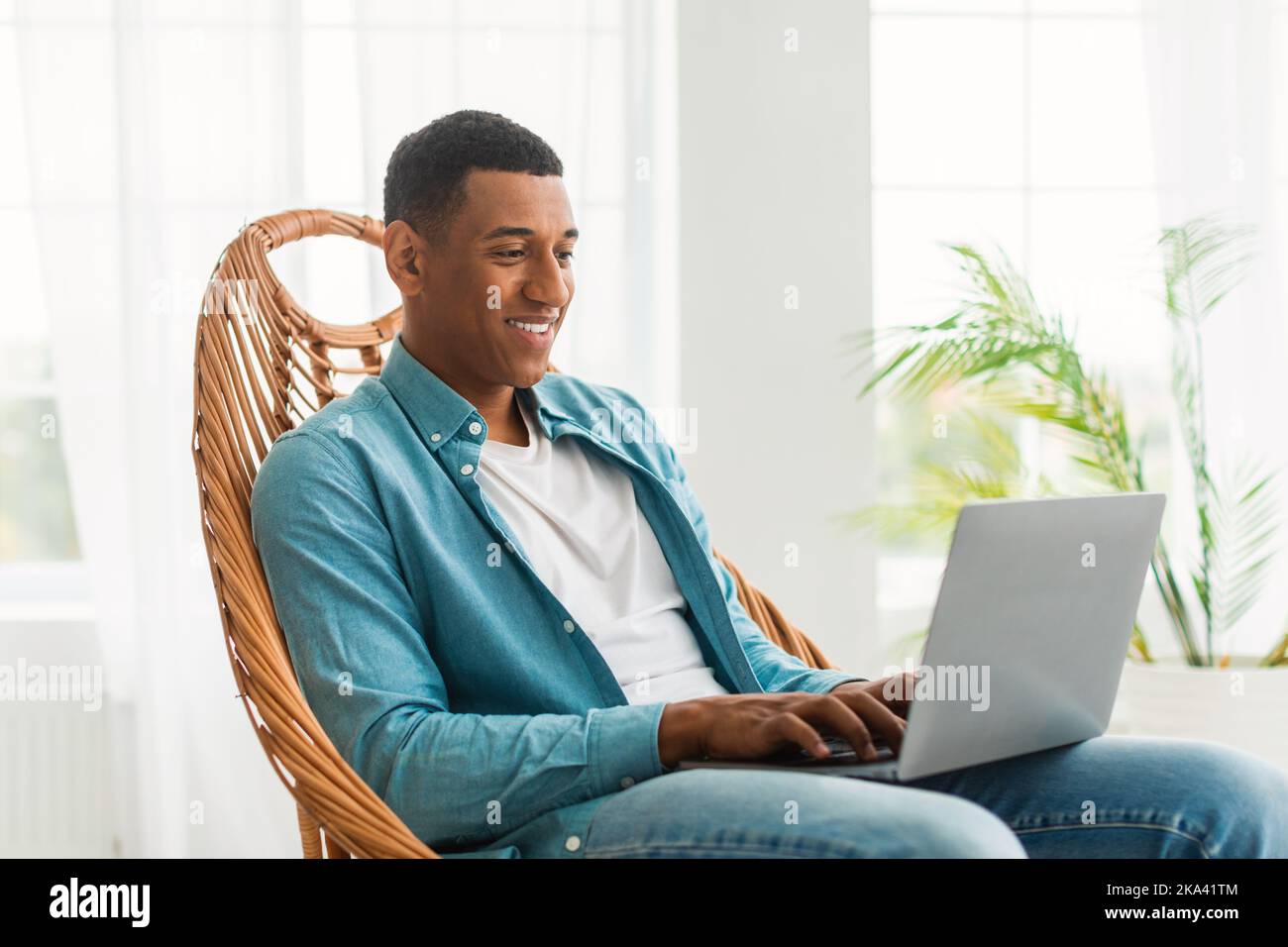 Happy young african american man typing, chatting on computer in light ...