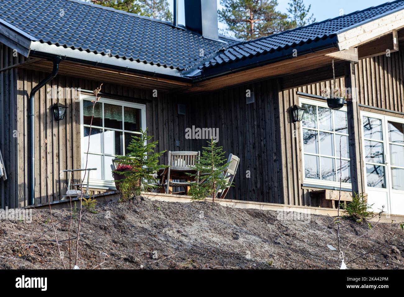 A closeup of a wooden rural building with a terrace and small fir trees ...
