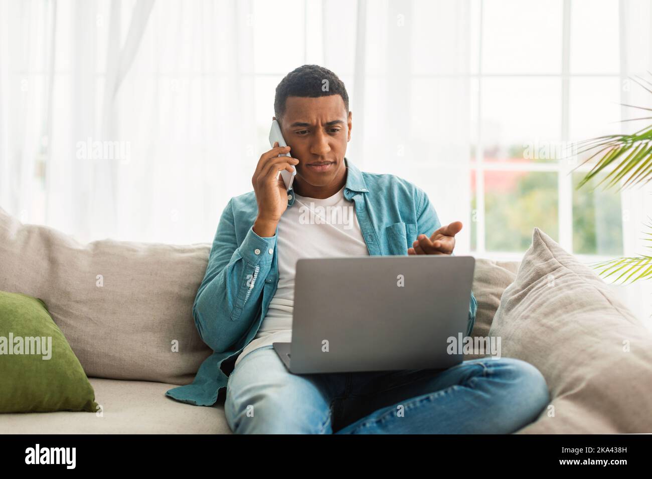Serious young african american man with computer calls by phone in ...