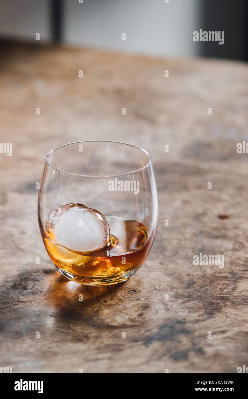 glass dram of whiskey whisky with sphere ice on burl wood table Stock ...