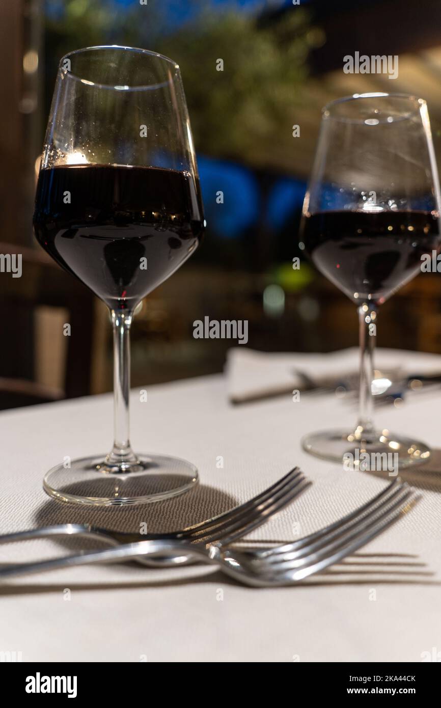A vertical closeup of the forks and glasses of red wine on the table ...