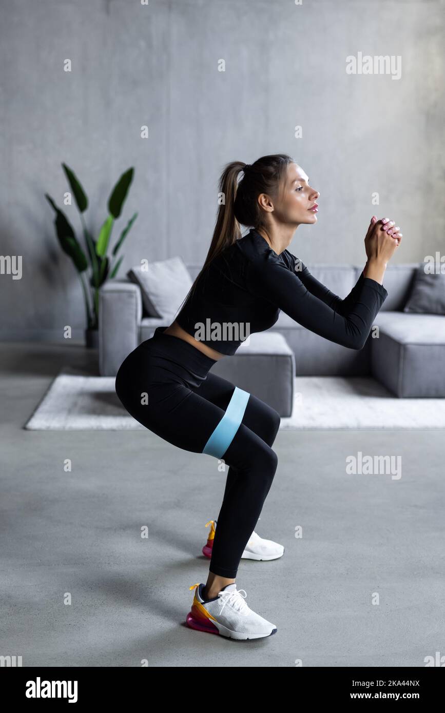 Home sports concept. Girl doing squats with elastic band in living room ...