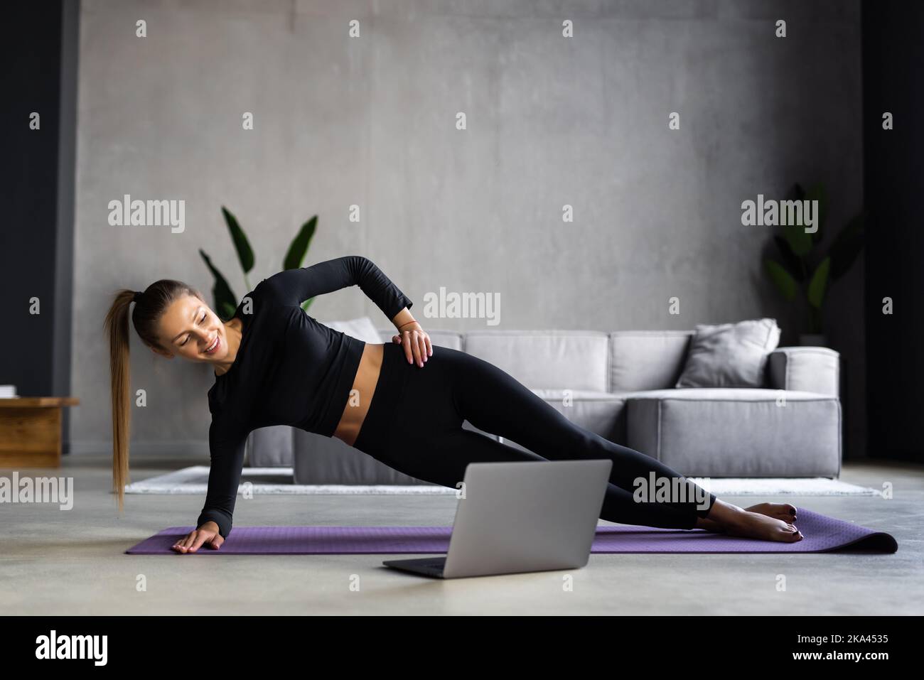 Beautiful sporty cheerful woman is doing side plank exercise. She is watching video on the ...