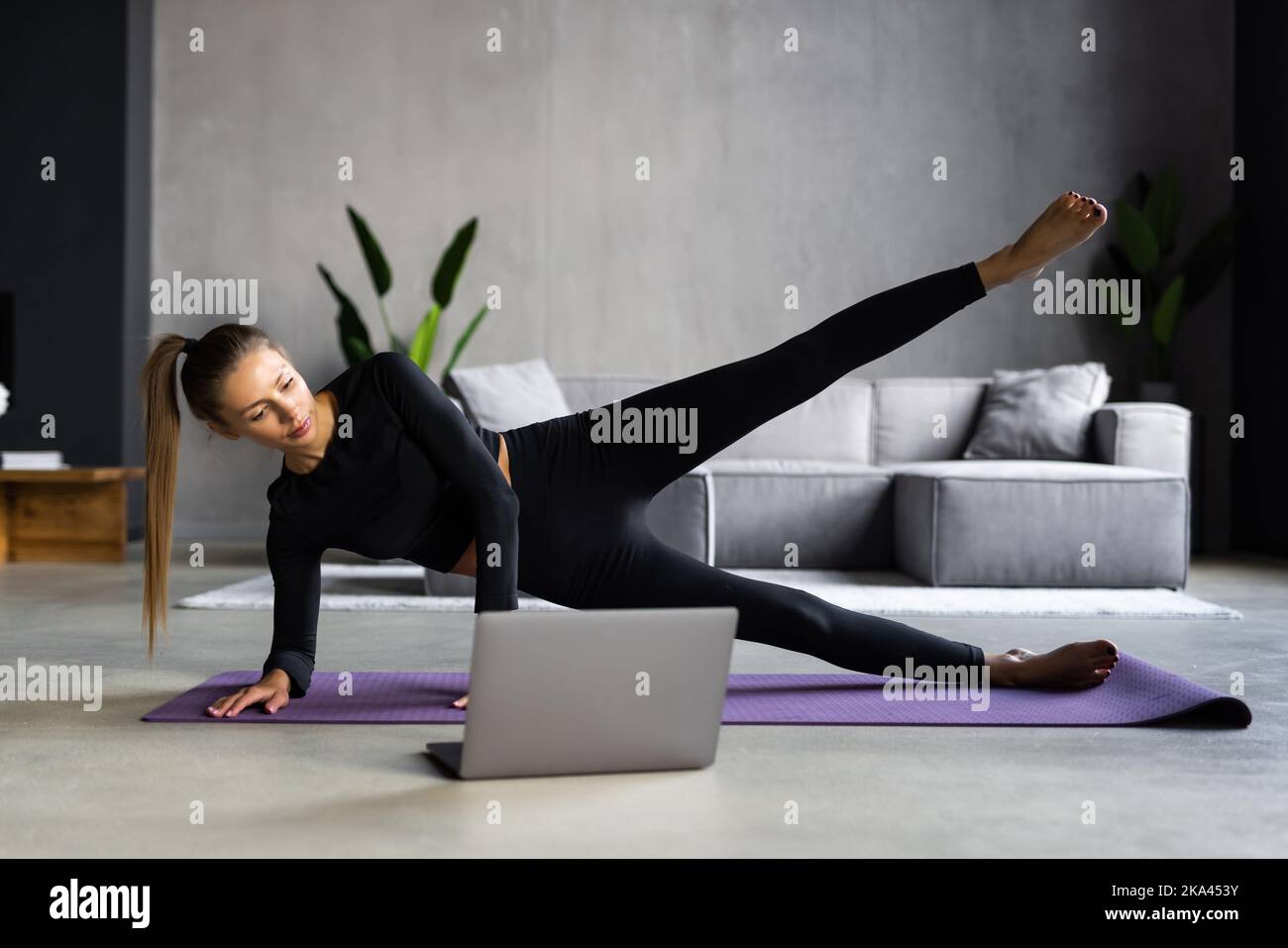 Beautiful sporty cheerful woman is doing side plank exercise. She is watching video on the ...