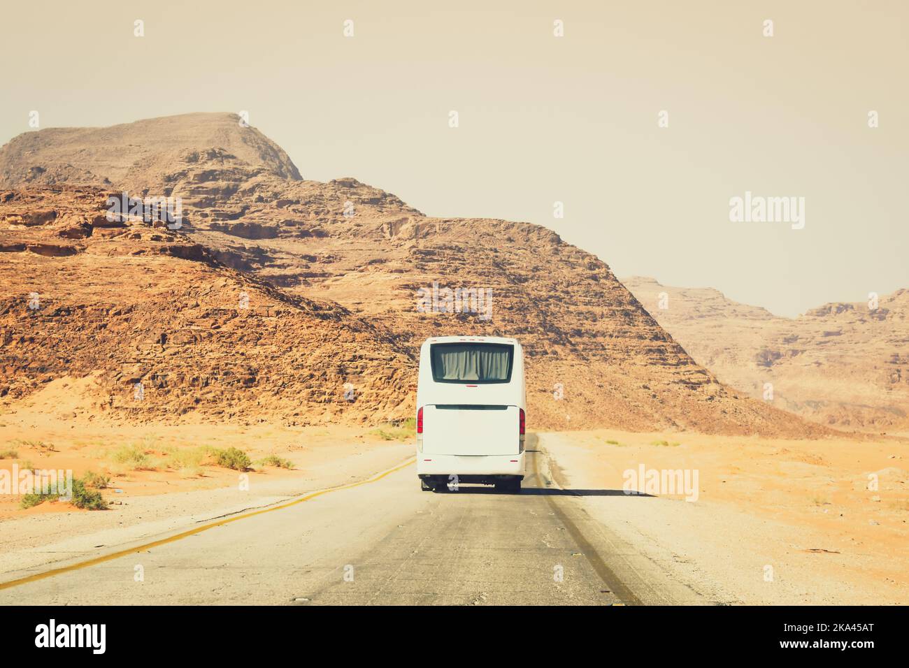 Back view white coach bus drive on asphalt road in scenic Wadi rum ...