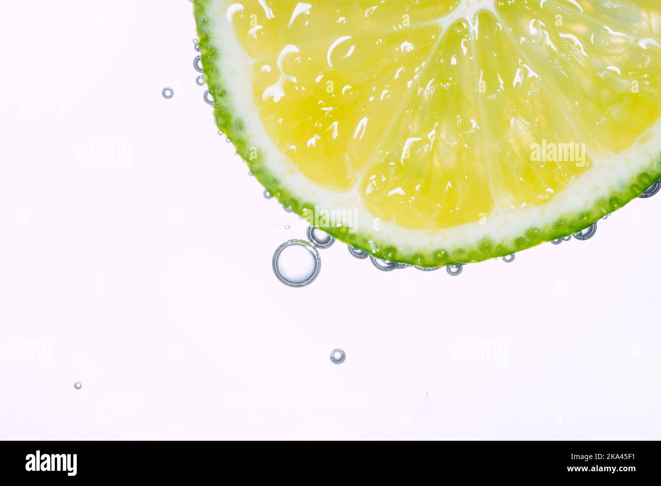 Macro photo of lime slice In soda water with bubbles isolated on white background. Freshness and ...