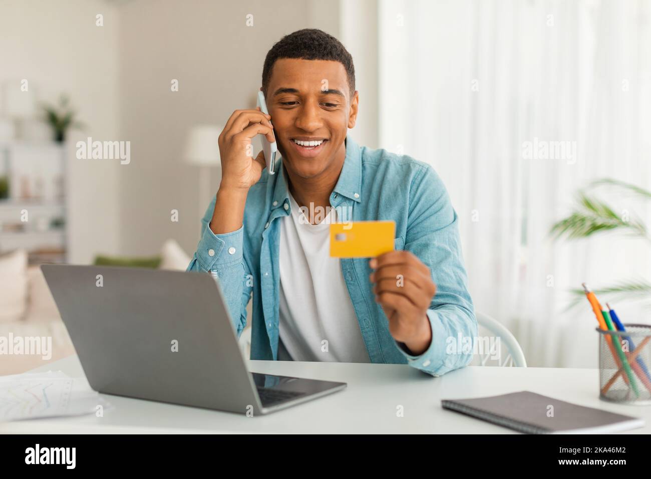Smiling millennial african american guy calling by phone, uses credit ...